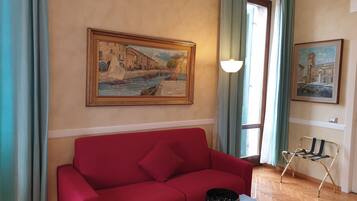 Um quarto com um sofá vermelho, uma mesa de centro de madeira, uma tigela preta e duas pinturas na parede.