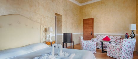 Quarto de hotel com uma cama grande, televisão, sofá e uma mesinha.