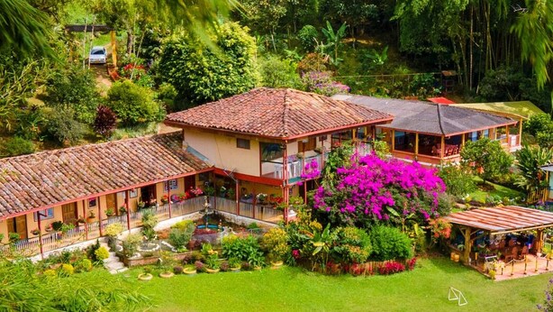Uma casa de dois andares com telhado em telhas, rodeada por jardins exuberantes e flores vibrantes.