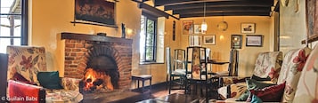 Um quarto aconchegante com lareira, móveis com padrão floral e quadros nas paredes.
