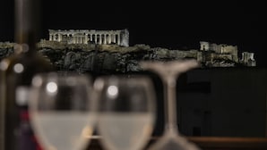 Vista da Acrópole à noite, com duas taças de vinho em primeiro plano.