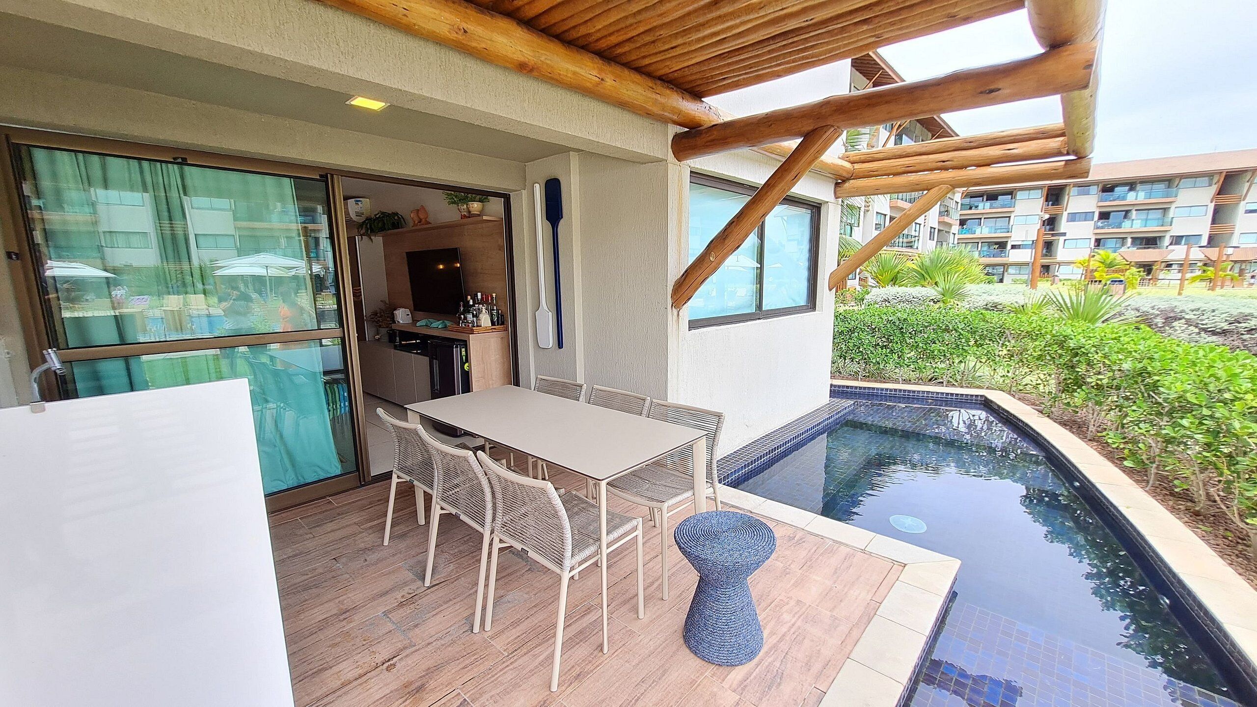 Uma área externa coberta com piscina, mesa de jantar com cadeiras e cozinha.