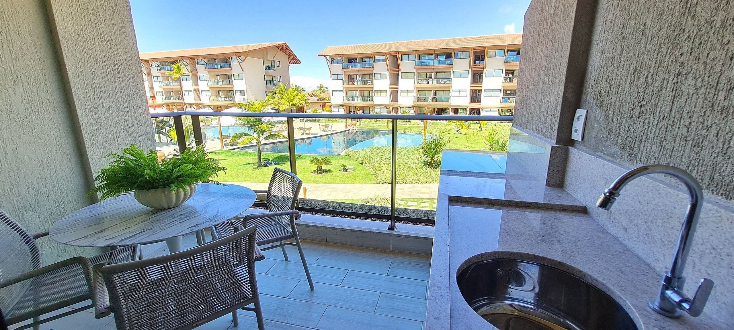 Varanda com mesa, cadeiras, pia e vista para uma piscina e edifícios de apartamentos.