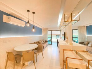 Quarto de hotel moderno com área de jantar, sofás e vista para o exterior.
