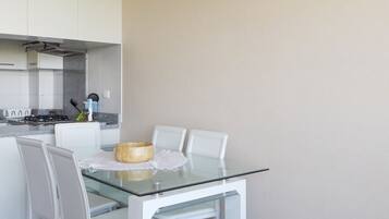 Uma cozinha moderna com armários brancos, uma mesa de jantar de vidro e cadeiras brancas.