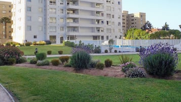Edifício residencial com vários andares e varandas, cercado por gramados e arbustos bem cuidados.