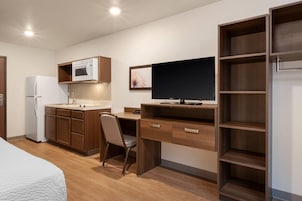 Quarto de hotel compacto com cozinha compacta, cama, escrivaninha e cadeira, e televisão.