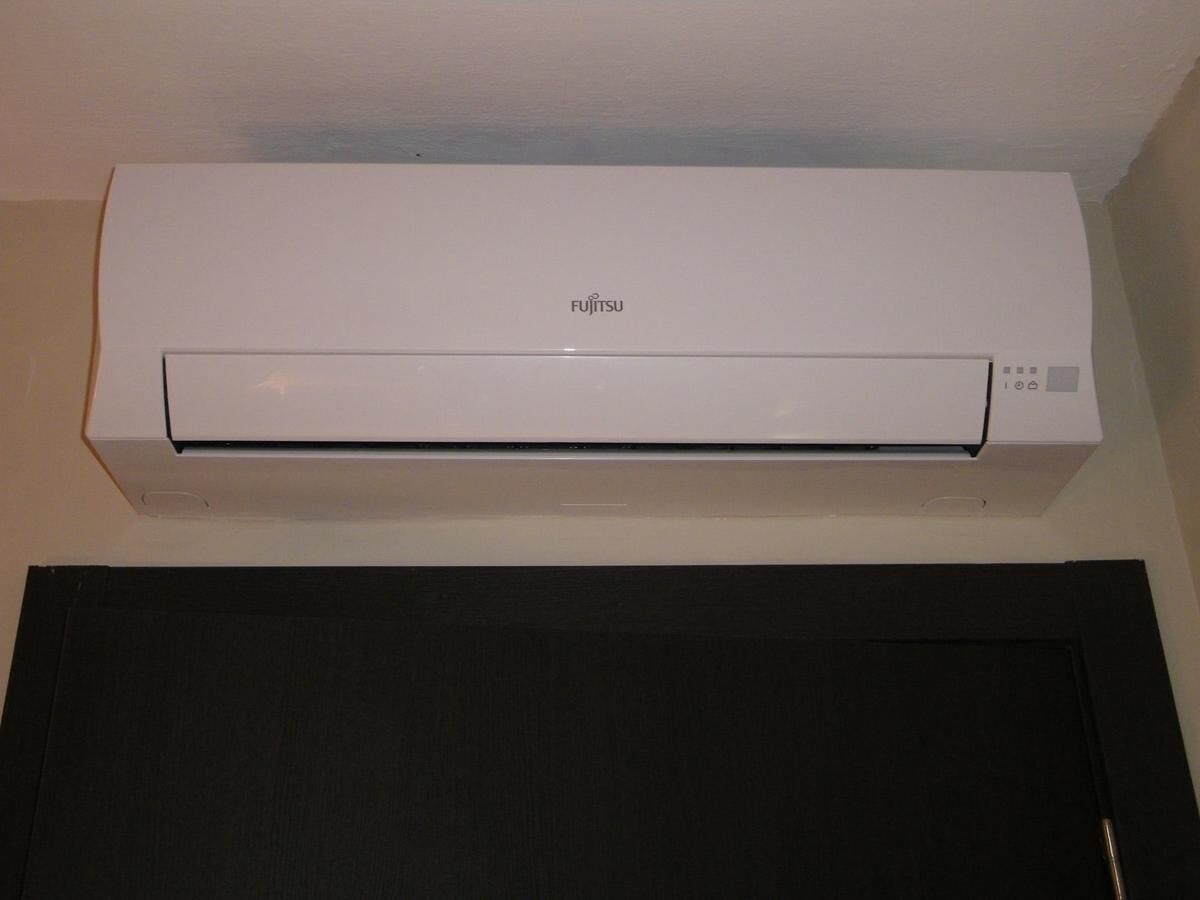 Ar condicionado branco da Fujitsu fixado na parede acima de uma porta escura.