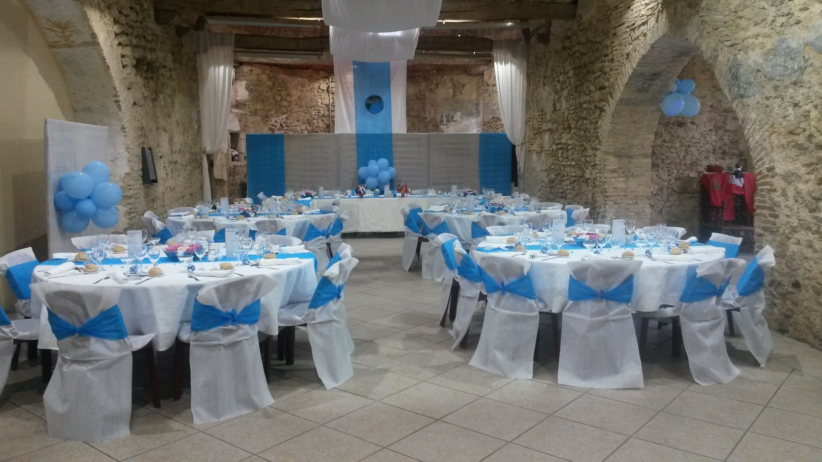 Salão de banquetes com mesas redondas preparadas para um evento formal, com toalhas brancas e fitas azuis.