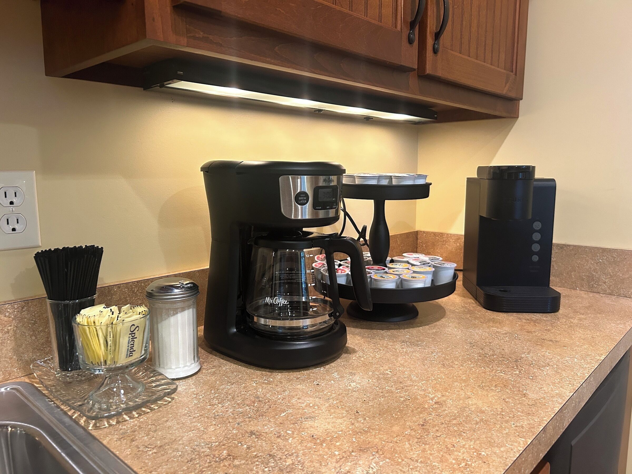 Uma cozinha com cafeteira, balança e recipientes de cápsulas de café.