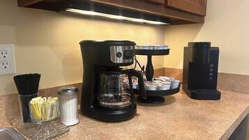 Uma cozinha com cafeteira, balança e recipientes de cápsulas de café.