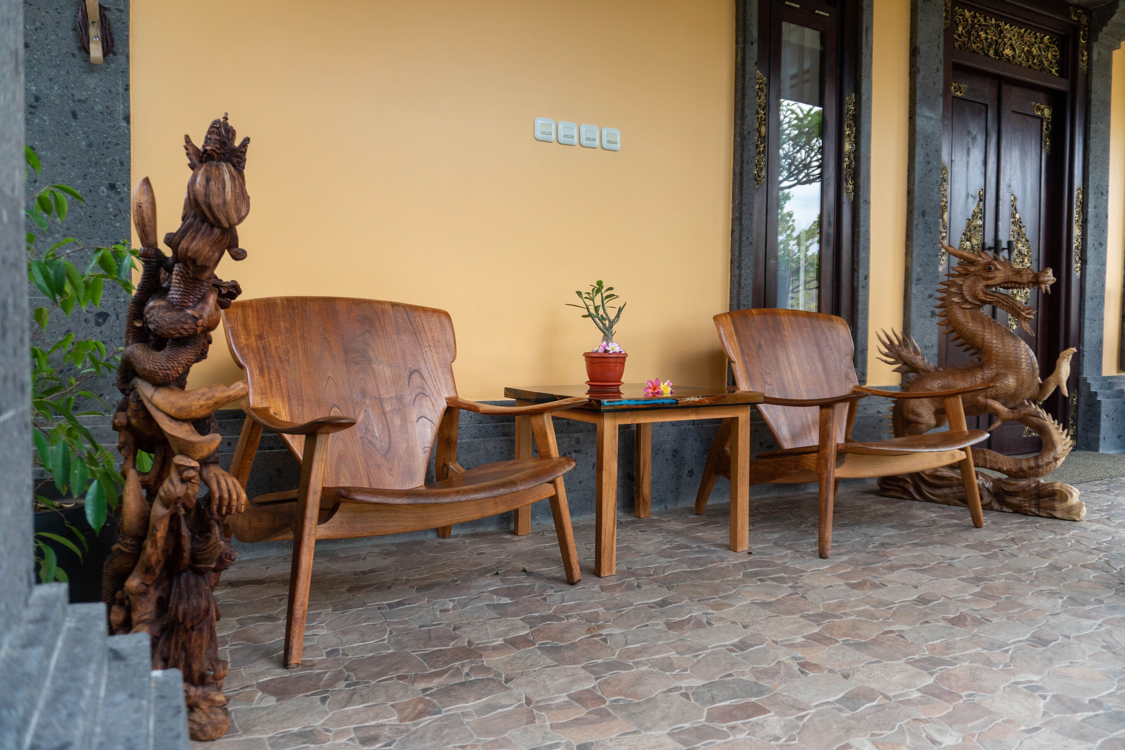 Uma área de estar ao ar livre com bancos de madeira, uma mesa, uma escultura decorativa de dragão e um vaso com planta.