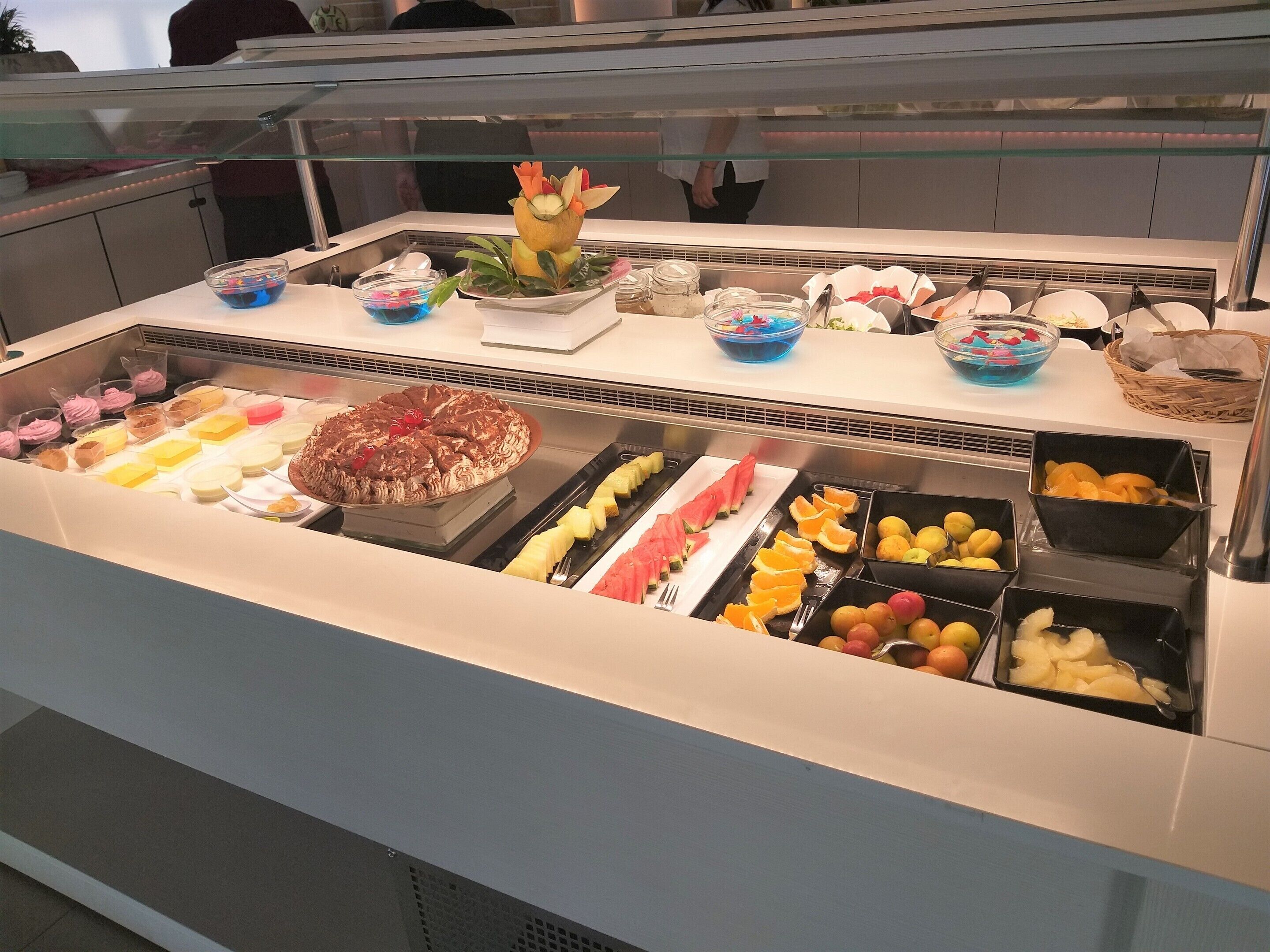 Buffet com diversos alimentos, incluindo um grande bolo de chocolate, frutas e sobremesas.