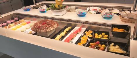 Buffet com diversos alimentos, incluindo um grande bolo de chocolate, frutas e sobremesas.