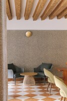 Um interior moderno com piso xadrez, uma mesa de madeira redonda, dois sofás com almofadas estampadas e uma parede com textura.