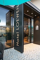Exterior do Hotel Loewen, com design moderno, apresentando uma entrada de vidro e áreas de estar visíveis no interior.