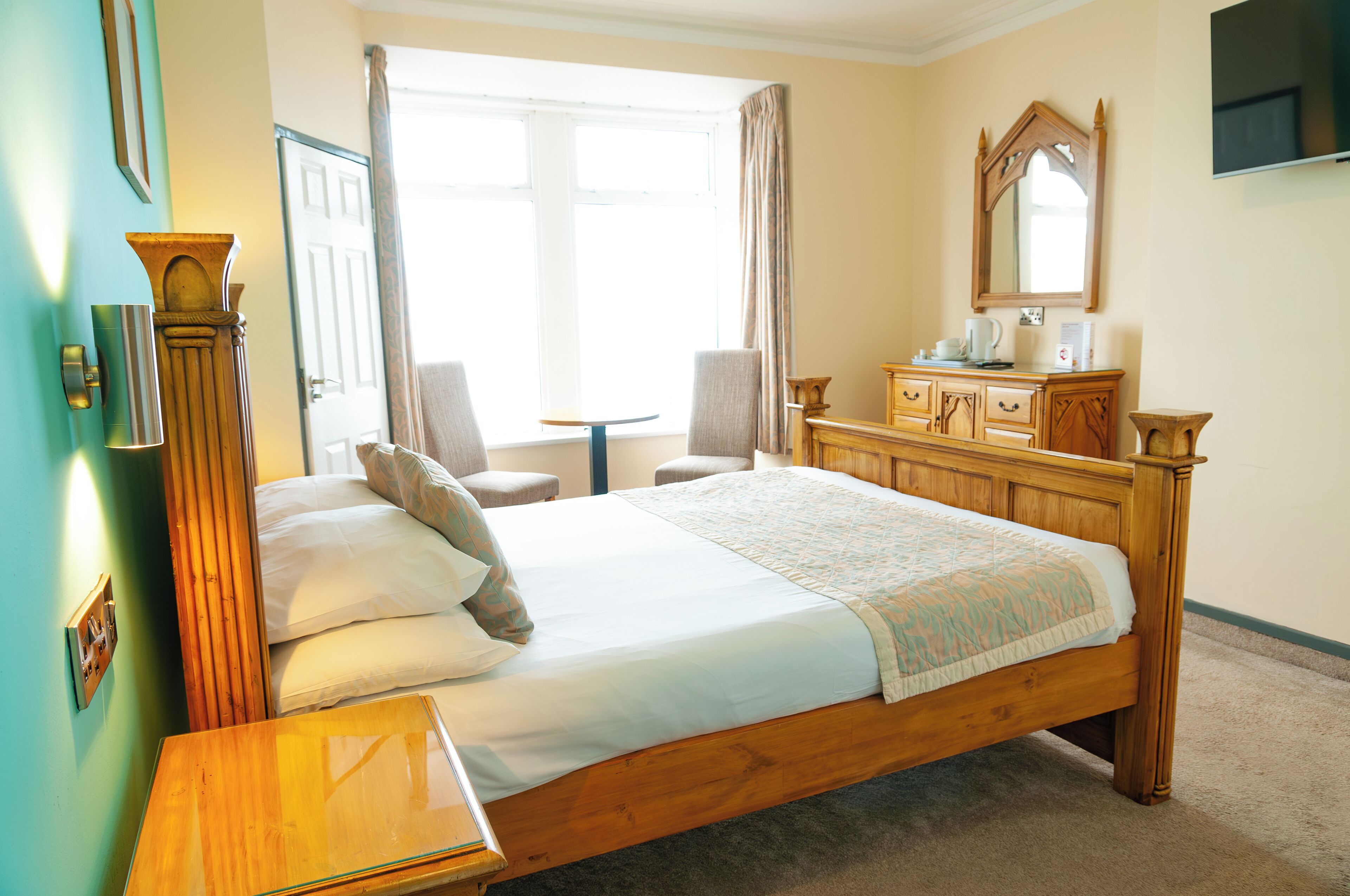 Quarto bem arrumado com cama de madeira, uma mesinha, uma cadeira e um armário.