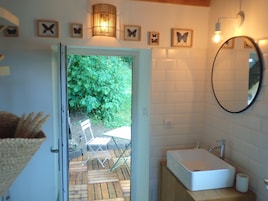 Casa de banho com lavatório branco, espelho e porta que dá para uma área exterior com mesa e cadeiras.