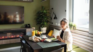 Uma sala de estar moderna com lareira, uma mesa de jantar com itens de café da manhã e uma grande janela com plantas.