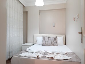 Uma cama bem arrumada com almofada estampada, mesa de cabeceira e luminária fixada na parede.