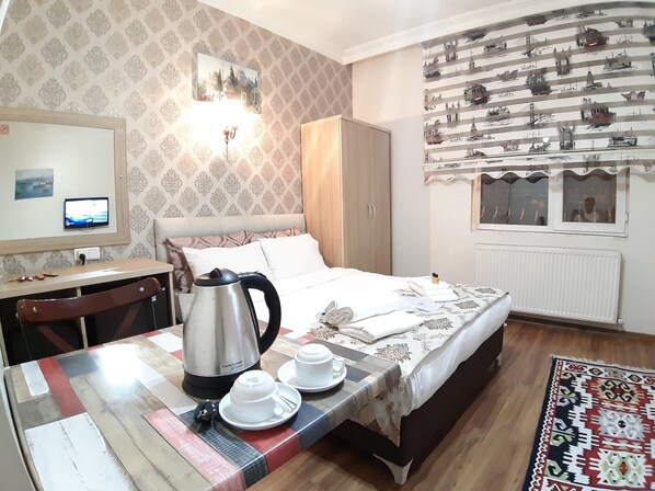 Quarto de hotel bem organizado com uma cama, uma escrivaninha, uma chaleira e uma mesa posta com xícaras e um prato.