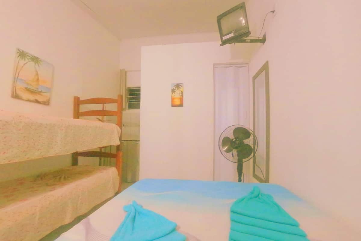 Quarto com beliches, um ventilador e televisão na parede.