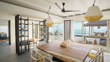Uma sala de jantar espaçosa com uma grande mesa de madeira e cadeiras amarelas, com vista para uma praia.
