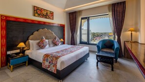 Quarto de hotel com uma cama grande, uma mesa de cabeceira, uma cadeira, uma janela com vista e um quadro na parede.