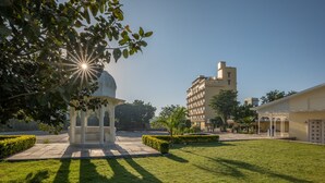 Um pátio bem cuidado com um coreto central, um edifício grande com cúpula e uma construção moderna com varandas.