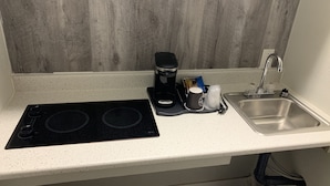 Uma cozinha compacta com um fogão por indução preto, uma cafeteira, uma caneca e uma pia.