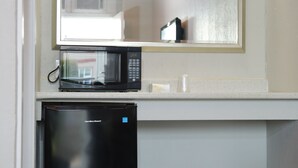 Uma cozinha compacta equipada com micro-ondas, pequena geladeira e espelho sobre o balcão.