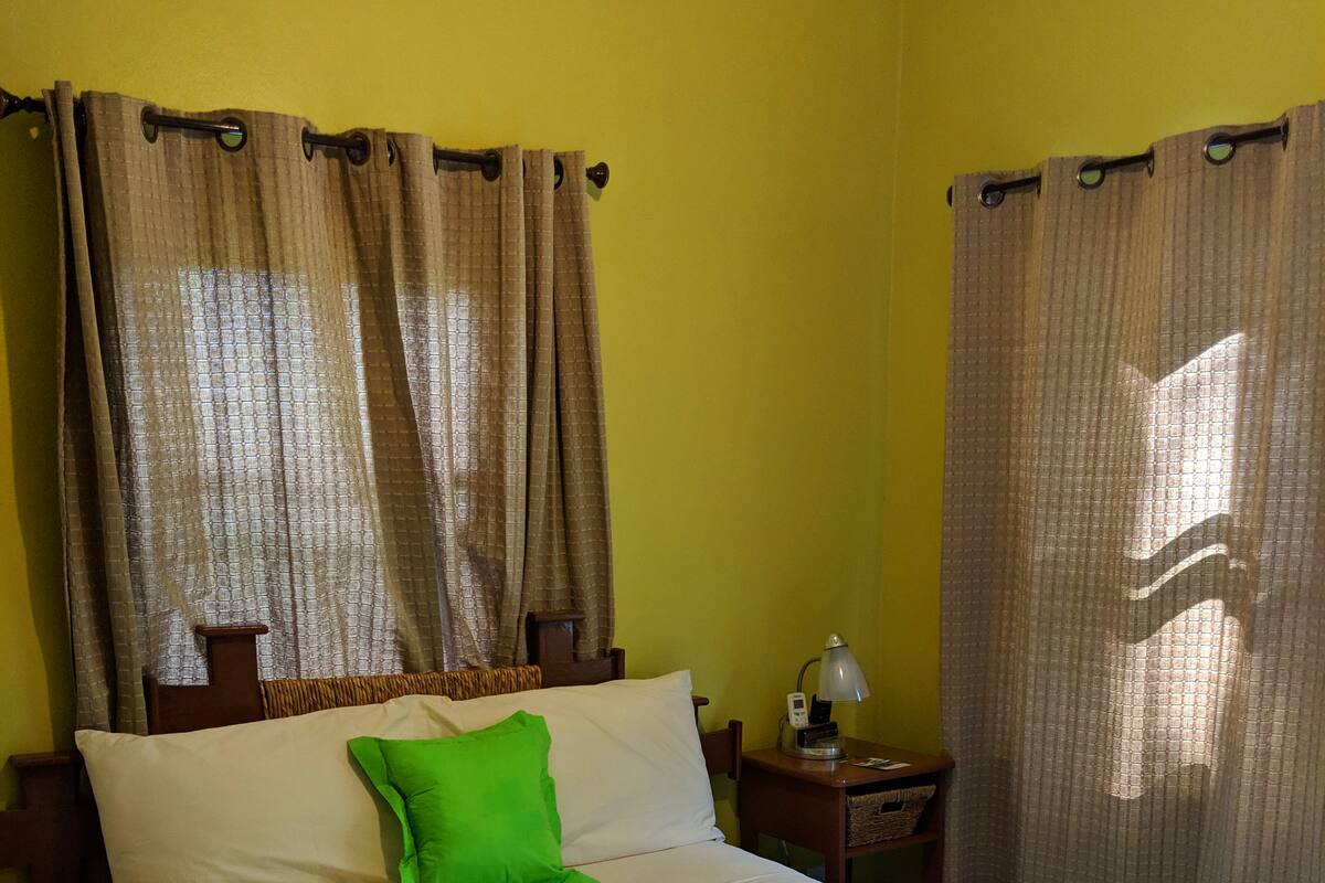 Cama bem arrumada com um travesseiro verde, uma toalha enrolada e um folheto sobre a cama.