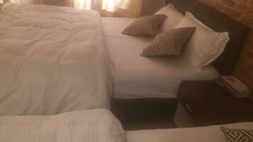 Quarto de hotel com duas camas, cada uma com almofadas estampadas e cabeceira de madeira.