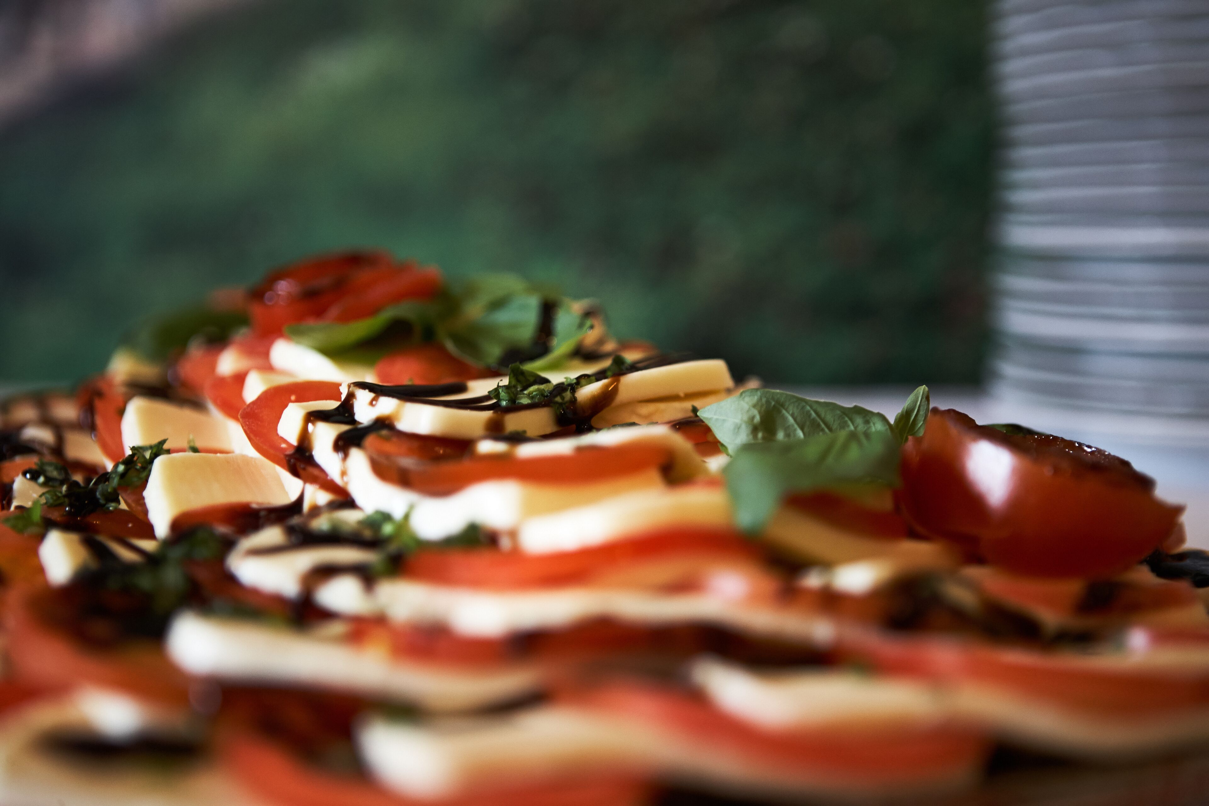 Um close-up de um prato em camadas com tomate, queijo e folhas verdes.