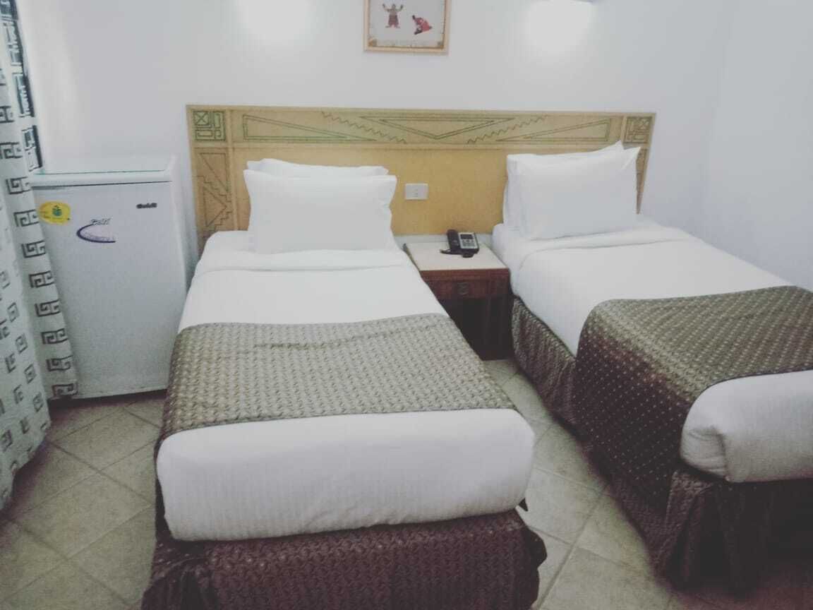 Quarto de hotel com duas camas de solteiro, um pequeno frigorífico, mesa de cabeceira com telefone e cortina estampada.