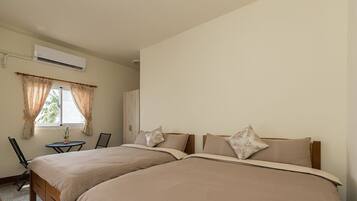 Quarto de hotel com duas camas, uma escrivaninha, ar condicionado e uma janela com cortinas.