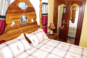 Quarto com cabeceira de madeira, cama com roupa de cama xadrez, abajur e espelho.