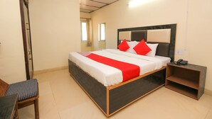 Quarto de hotel moderno com uma cama grande, uma cadeira de madeira e uma mesinha de cabeceira.