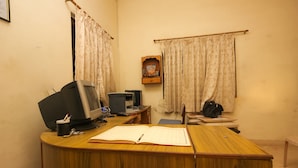 Quarto com escrivaninha de madeira, computador, televisão e um pequeno santuário na parede.
