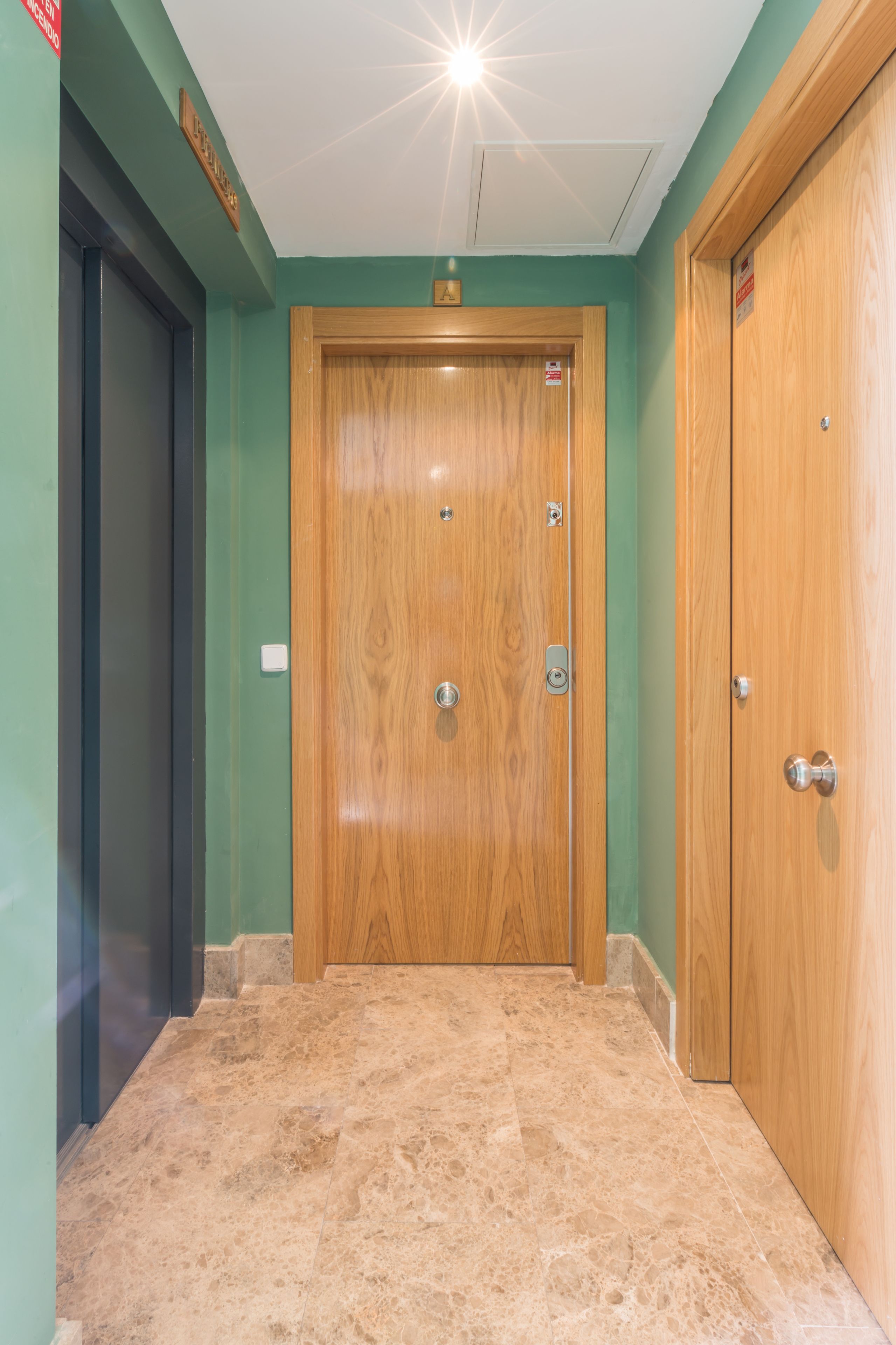 Um corredor com porta de madeira, interruptor de luz e um aviso na parede.