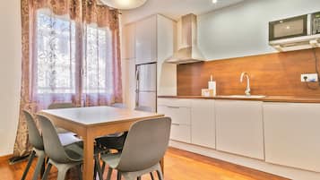 Uma cozinha moderna com armários brancos, bancada de madeira e micro-ondas embutido.