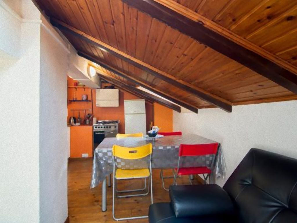 Uma sala de jantar com mesa e cadeiras, uma cozinha ao fundo e teto de madeira.