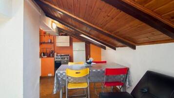 Uma sala de jantar com mesa e cadeiras, uma cozinha ao fundo e teto de madeira.