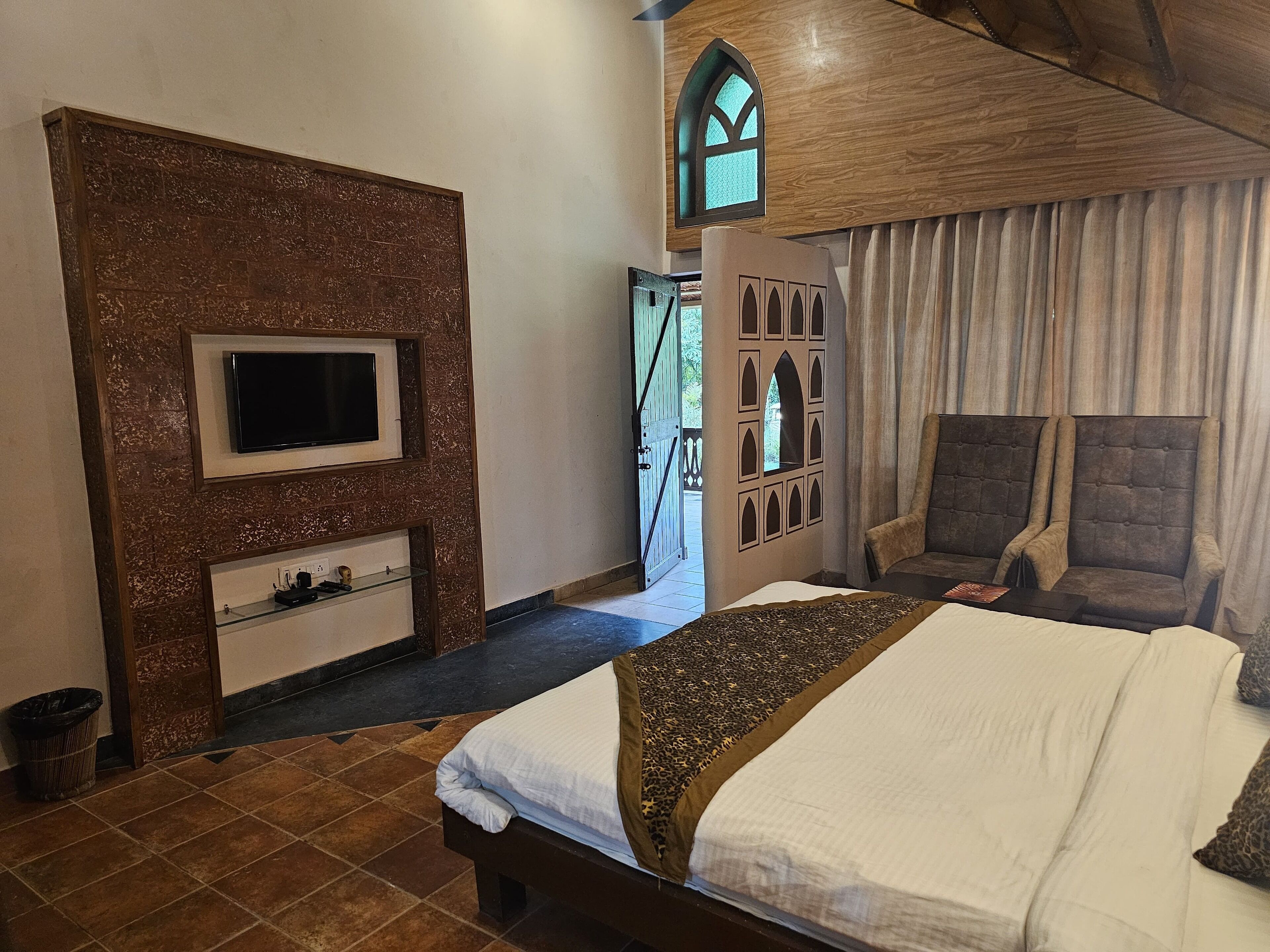 Quarto com cama, televisão presa numa parede texturizada, janela e cadeira.