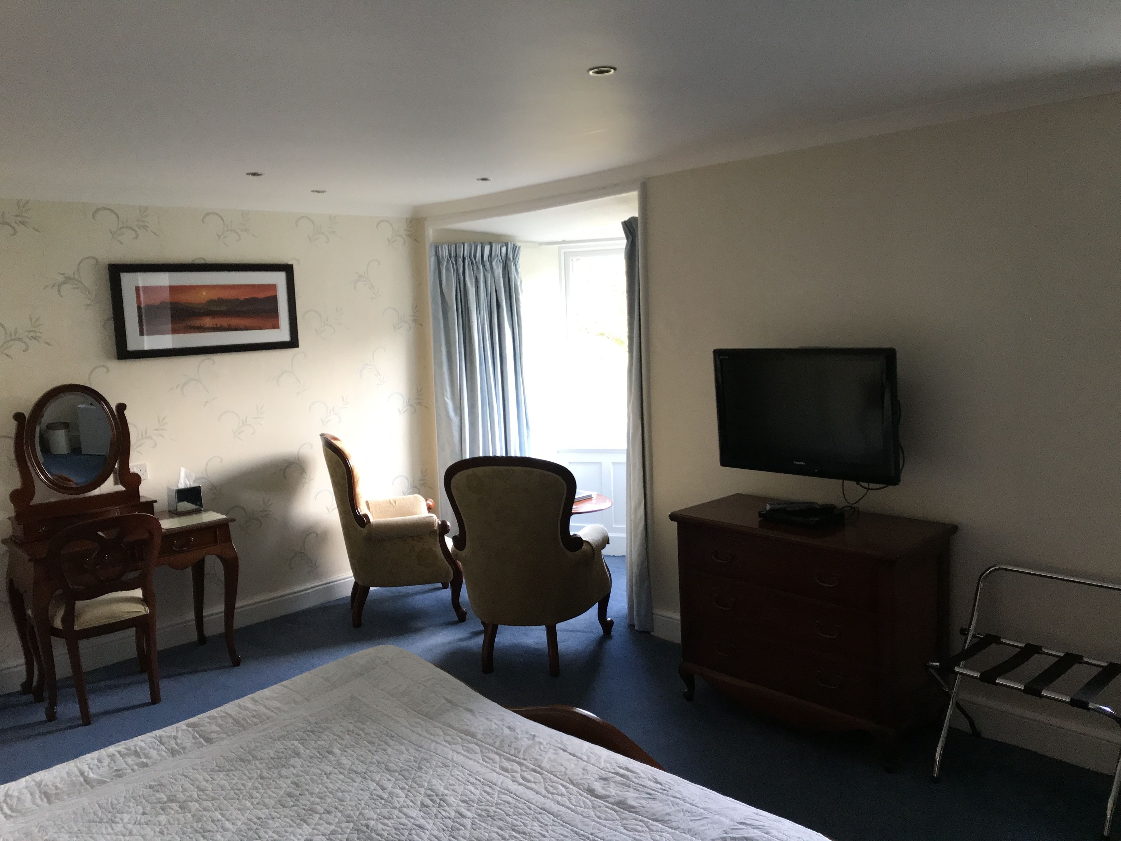 Quarto de hotel com cama, escrivaninha, cadeira, televisão e janela com cortinas.