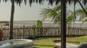 Uma área externa coberta com piscina, cadeiras de descanso e vista para a praia.