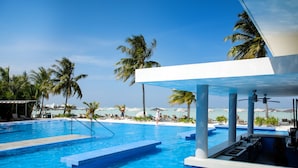 Uma área de piscina com água azul cristalina, palmeiras e vista para a praia.
