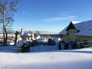 Uma área residencial coberta de neve, com casas e um prédio amarelo destacado, sob um céu azul límpido.