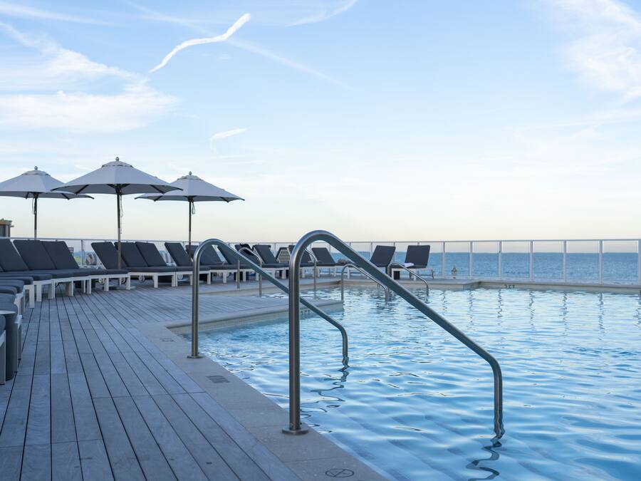 Uma área à beira da piscina com espreguiçadeiras e guarda-sóis, piscina e vista para o mar.