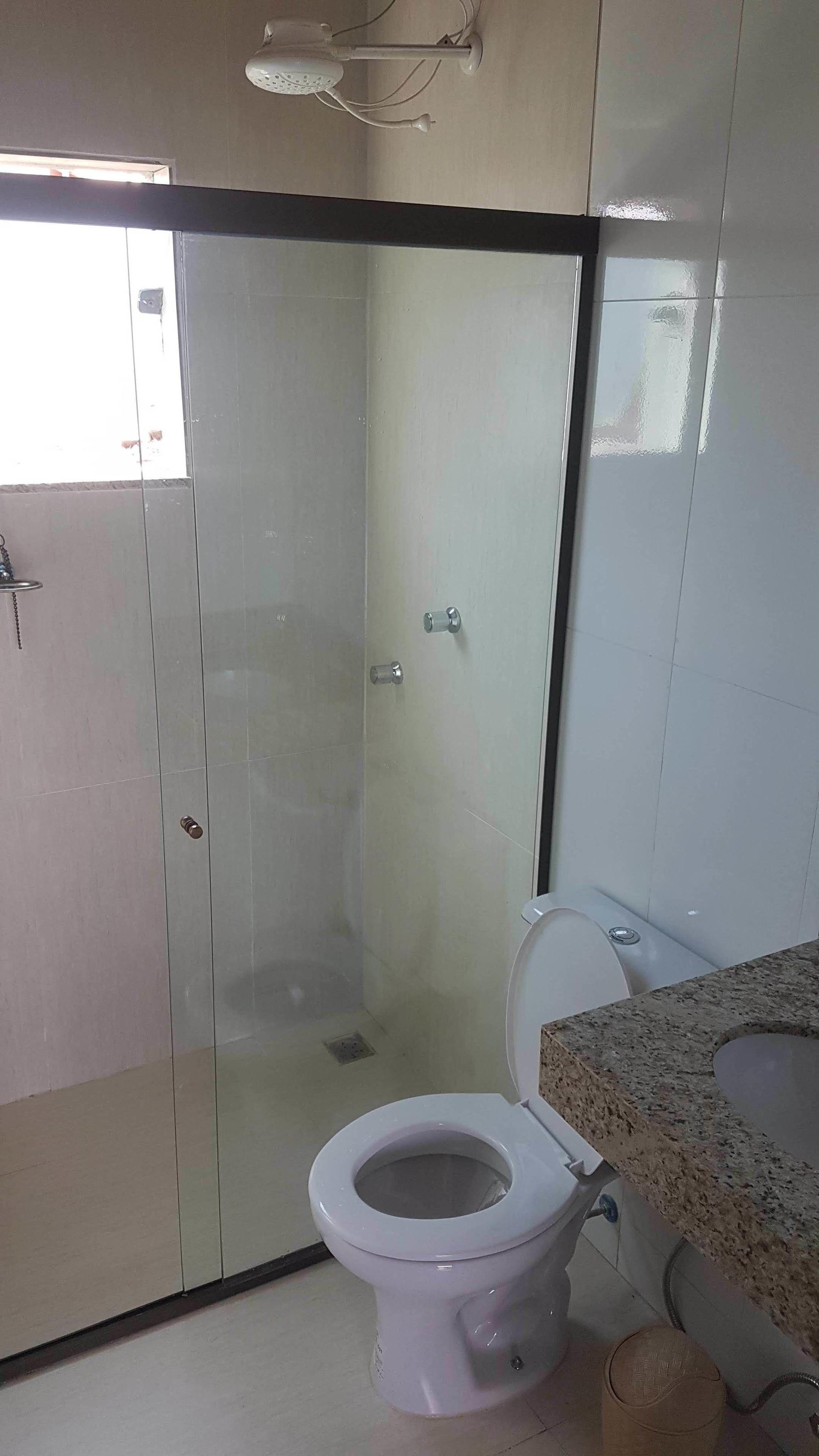 Um banheiro com chuveiro em box de vidro, vaso sanitário e bancada de granito.